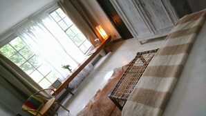 Quarto com uma janela grande, um banco de madeira, uma cesta de palha e um tapete estampado.