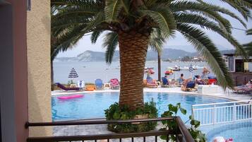Uma área à beira da piscina com espreguiçadeiras, uma palmeira e vista para o mar.
