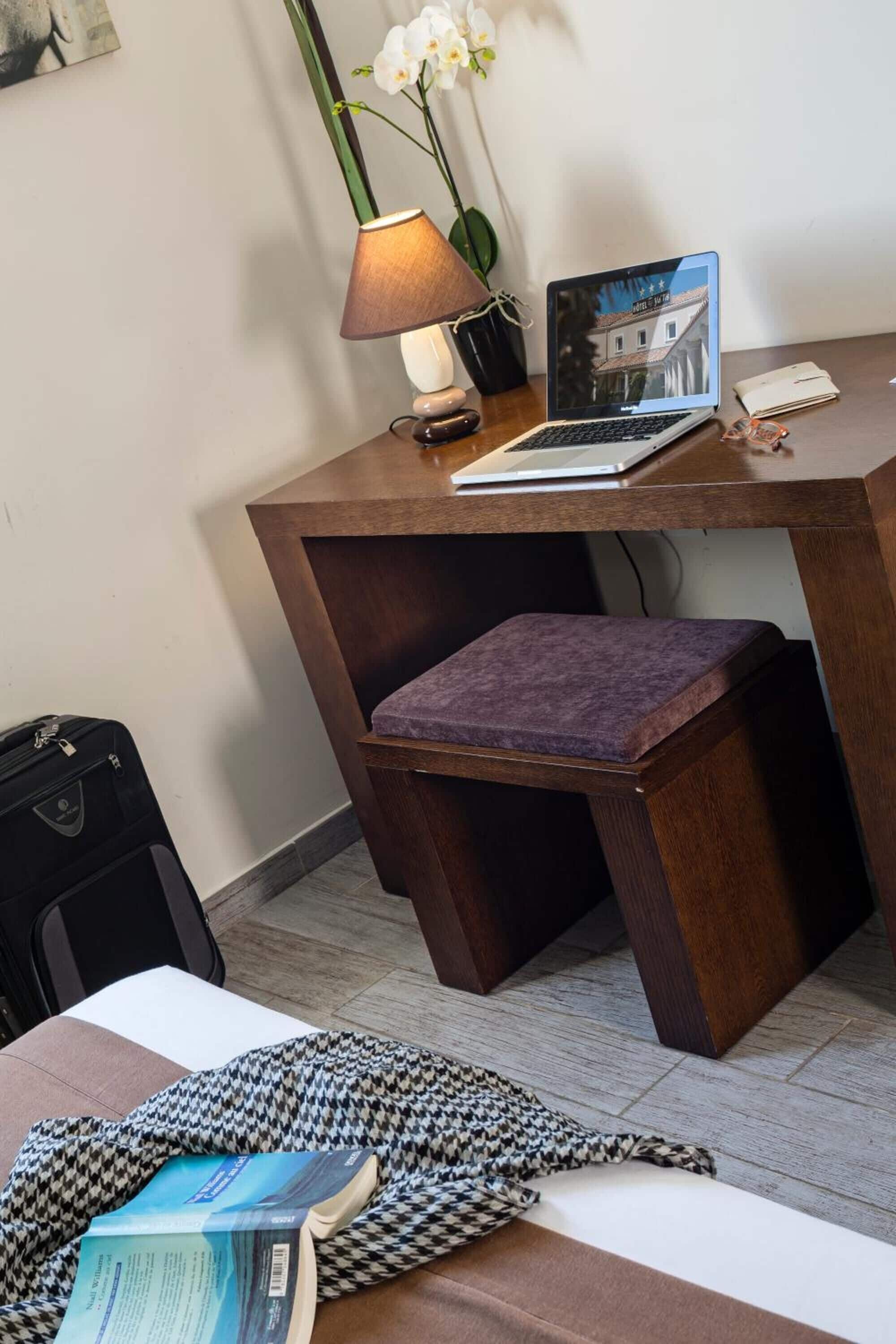 Uma mesa de madeira com um laptop, uma lâmpada e um vaso com flores.