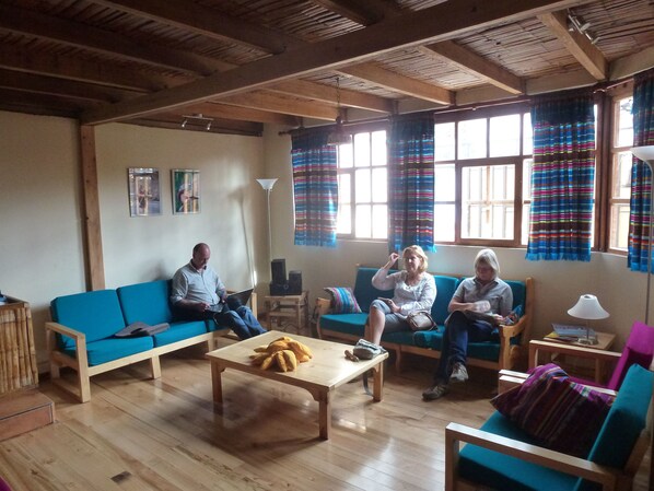 Uma sala de estar aconchegante com piso de madeira, um sofá azul, uma mesa de centro de madeira e janelas amplas com cortinas coloridas.