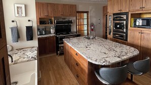 Uma cozinha com armários de madeira, bancada de mármore e uma ilha central com banquetas.