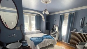 Um quarto com uma cama, cômoda, espelho, radiador e uma cadeira.