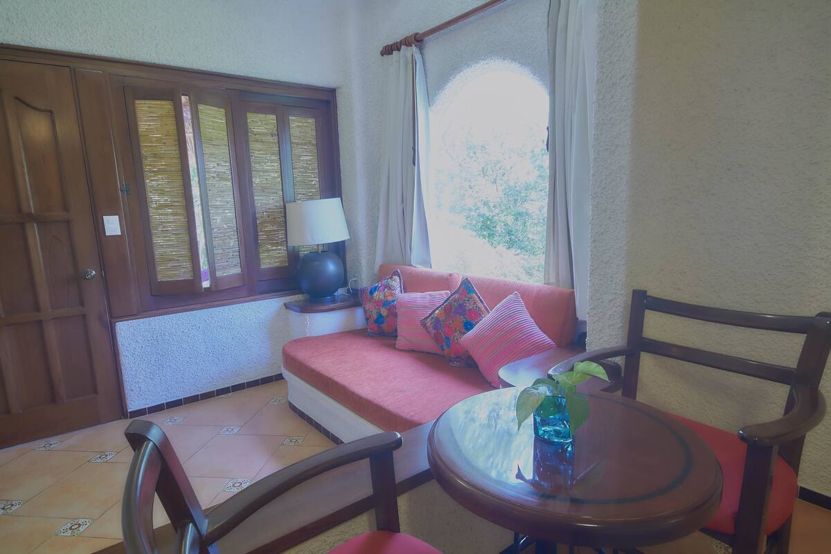 Um quarto aconchegante com sofá, cadeiras, uma mesinha e uma janela com cortinas.