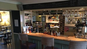 Uma área de bar com banquetas, balcão e diversos garrafas e copos.
