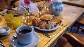 Uma mesa de pequeno-almoço com croissants, torradas, um bule de chá e uma chávena de café.