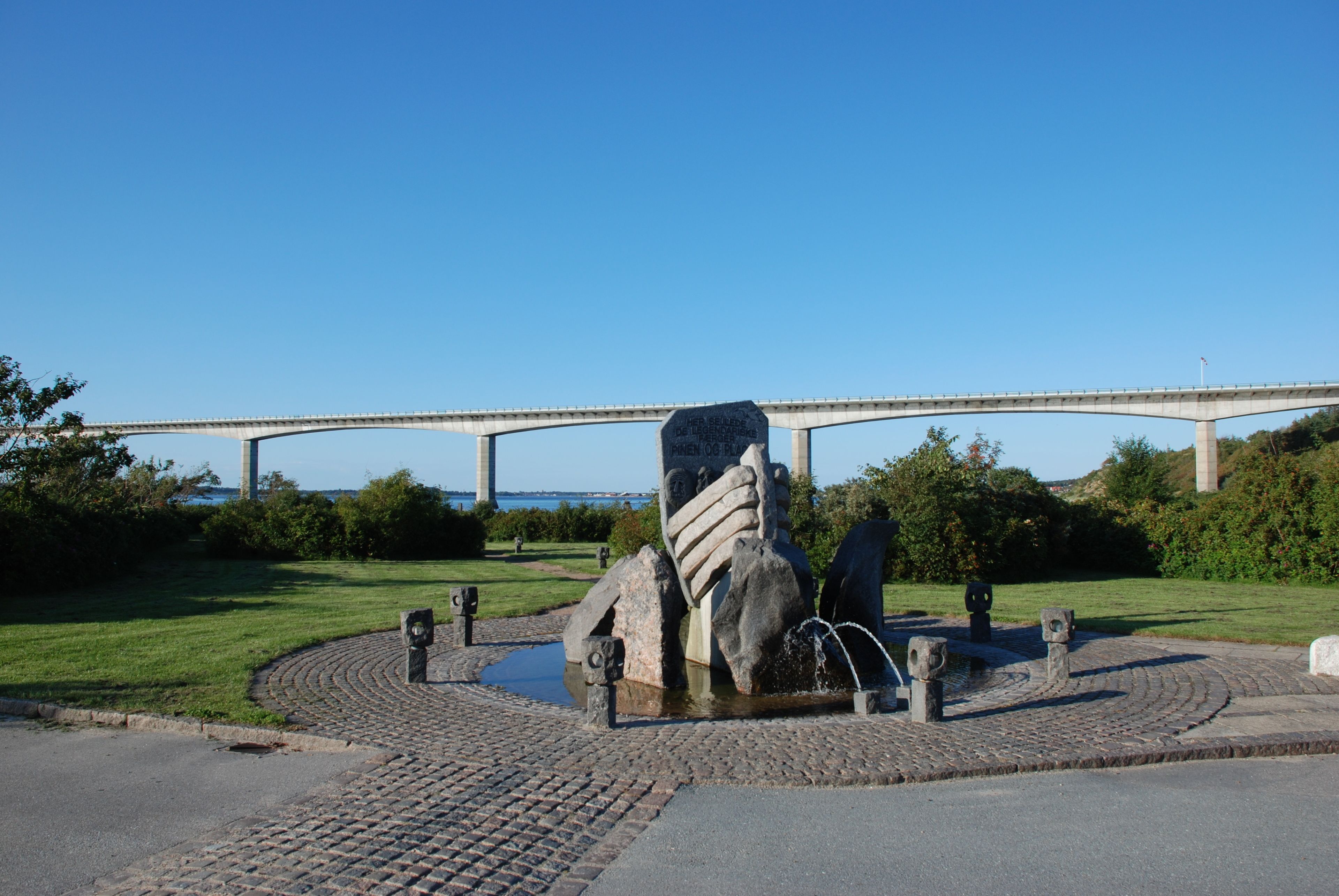 Uma escultura em um parque, com uma ponte ao fundo.