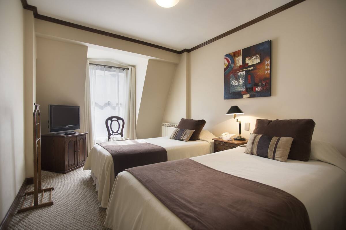 Quarto de hotel com duas camas, televisão, escrivaninha e um quadro na parede.