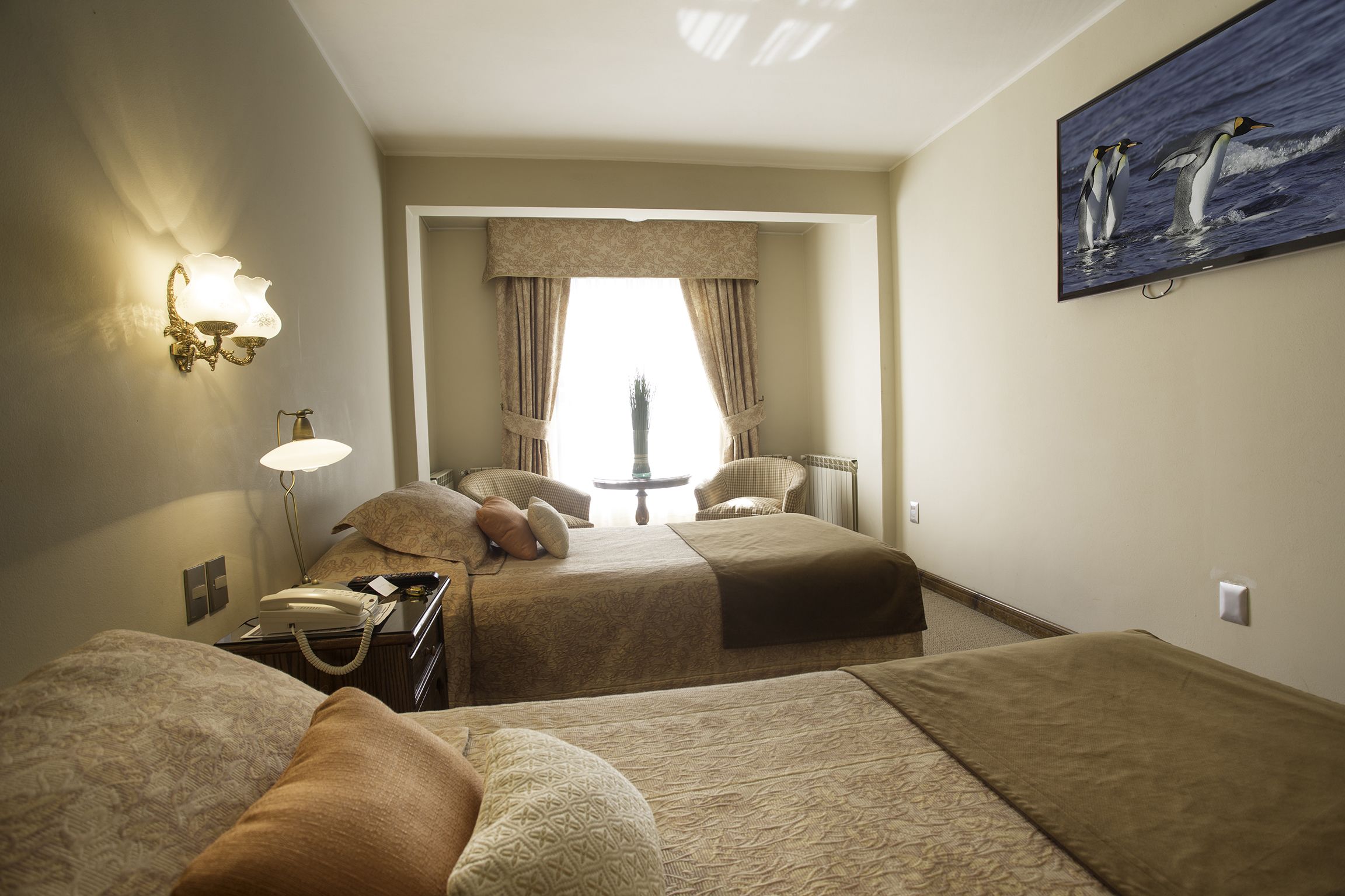 Quarto de hotel com duas camas, uma escrivaninha com telefone, uma luminária e um quadro na parede.