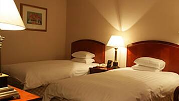Quarto de hotel com duas camas, cada uma com roupa de cama branca, cabeceira de madeira, mesas de cabeceira e luminárias.