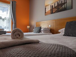 Quarto de hotel com duas camas, uma cabeceira de madeira, um quadro de um cais e uma janela com cortinas.