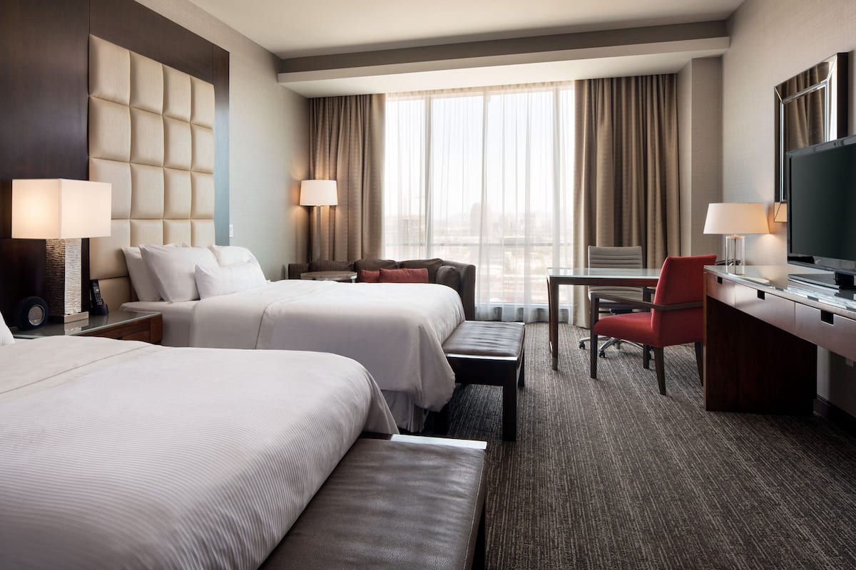 Quarto de hotel com duas camas, uma mesa, uma televisão e vista para a cidade.