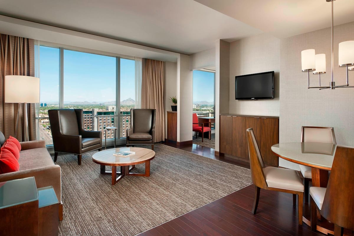 Quarto de hotel com uma janela grande, televisão de tela plana, mesa de jantar e duas cadeiras.