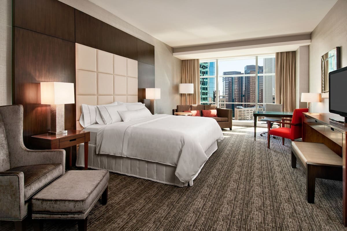 Quarto de hotel com cama grande, escrivaninha, cadeira e televisão.