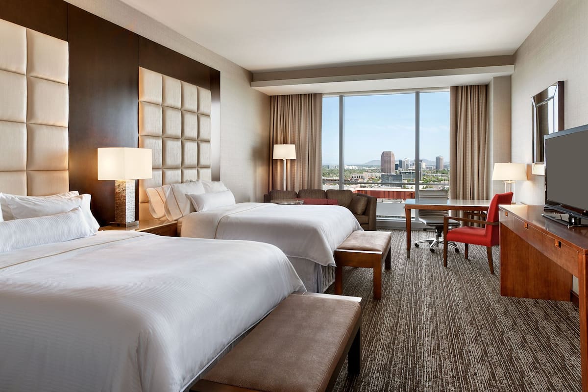Quarto de hotel com duas camas, uma escrivaninha, televisão e vista para a cidade.