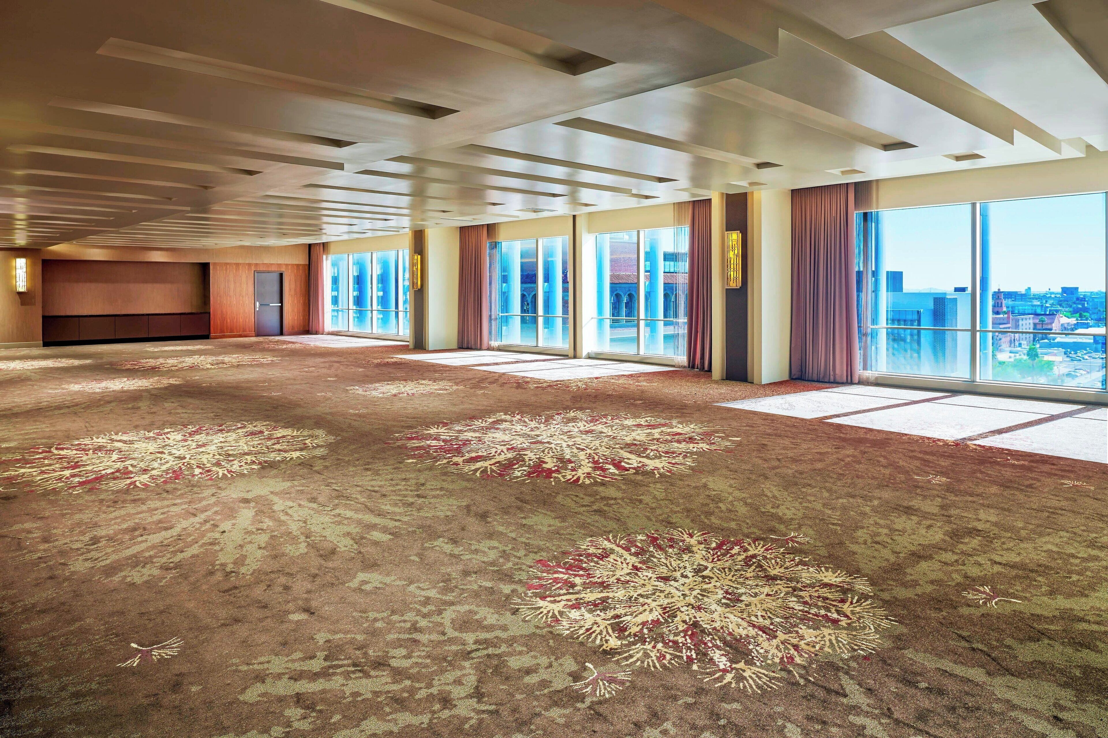 Quarto de hotel espaçoso com janelas amplas, carpete estampado e vista para a cidade.