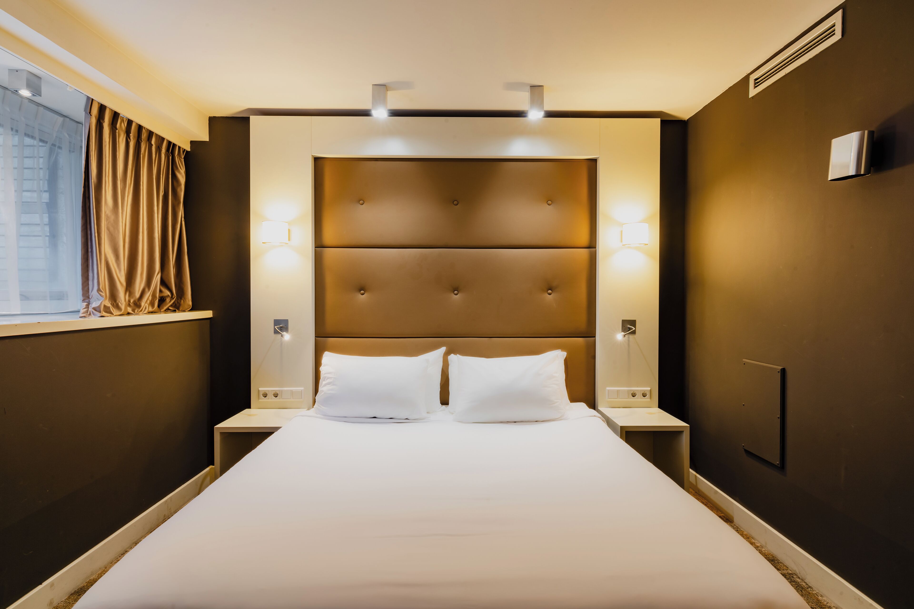 Quarto de hotel com uma cama grande, duas mesas de cabeceira e cabeceira com iluminação integrada.