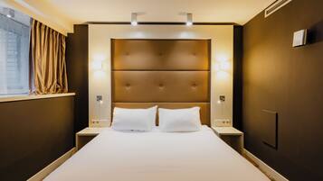 Quarto de hotel com uma cama grande, duas mesas de cabeceira e cabeceira com iluminação integrada.