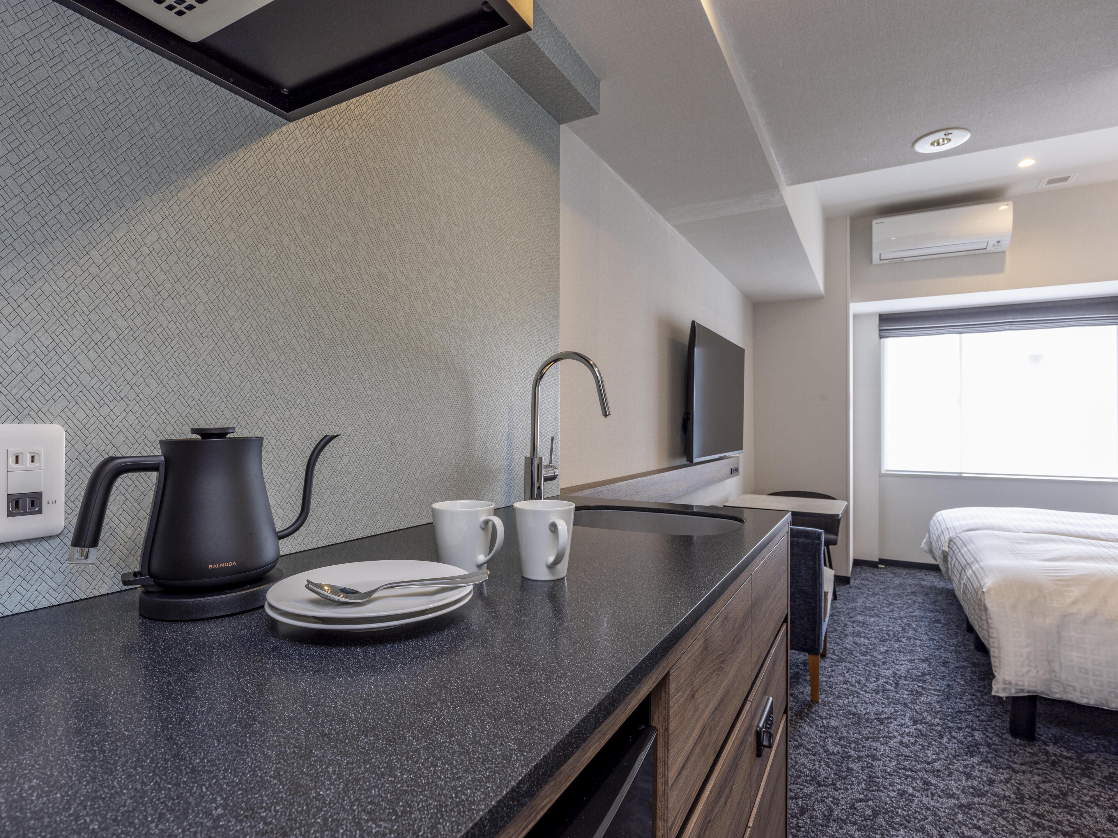 Quarto de hotel moderno com cozinha, cama e televisão.