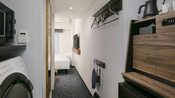 Quarto de hotel com cama, máquina de lavar, micro-ondas, cafeteira e armário de madeira.