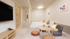 Quarto de hotel moderno com televisão de tela plana, mesa consola de madeira, mesa redonda com uma xícara, sofá e uma cadeira.