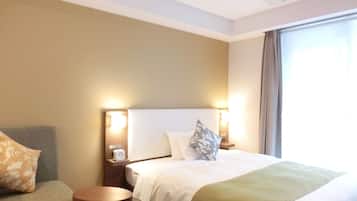 Quarto de hotel com cama, mesa de cabeceira, luminária, cadeira e janela com cortinas.