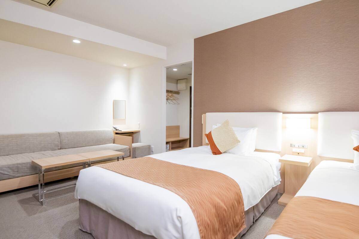 Quarto de hotel com duas camas, um sofá, uma escrivaninha e um espelho.