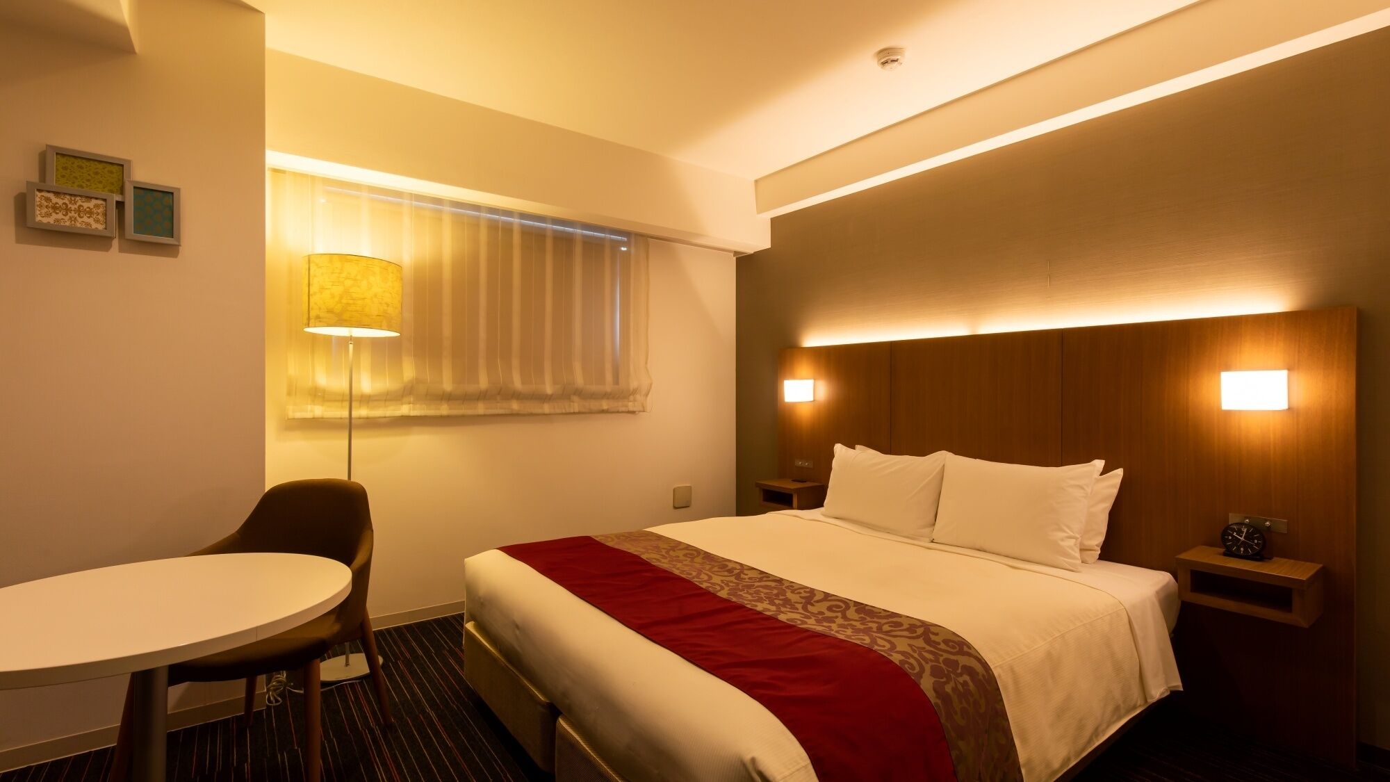 Quarto de hotel com cama, mesas de cabeceira, escrivaninha e uma cadeira.