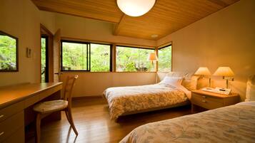 Quarto com duas camas, uma escrivaninha e uma cadeira. Janelas oferecem luz natural e vista para o verde lá fora.