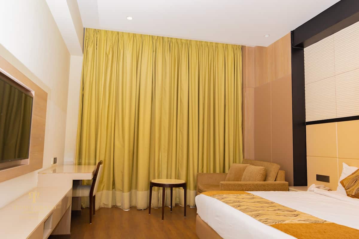 Quarto de hotel com cama, escrivaninha, cadeira e televisão.