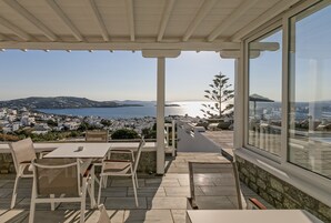 Uma área de estar coberta ao ar livre com vista para uma vila costeira e o mar.