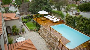 Piscina no terraço com espreguiçadeiras e um muro de pedra.