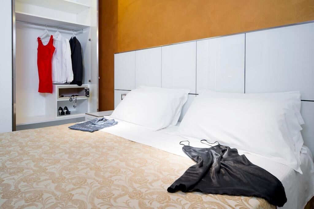 Quarto de hotel com uma cama, um guarda-roupa cheio de roupas penduradas e um escorredor de sapatos.