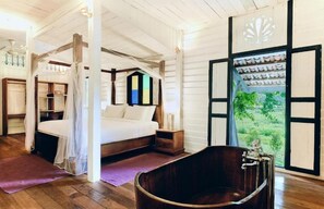 Quarto com cama de dossel, banheira de madeira e vista para o verde lá fora.