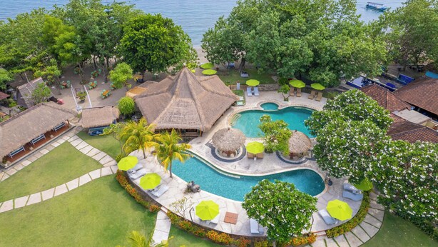 Um resort com piscina central, áreas de descanso e estruturas com telhado de palha.