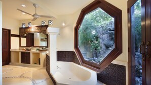 Casa de banho com uma banheira grande, toucador com espelho e janela com vista para um jardim.