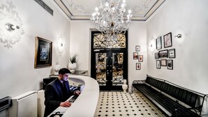 Uma área de recepção com lustre, piso em padrão preto e branco, um banco e quadros nas paredes.