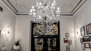 Um lustre imponente com várias luzes, um aplique decorativo e uma porta preta com desenhos elaborados.
