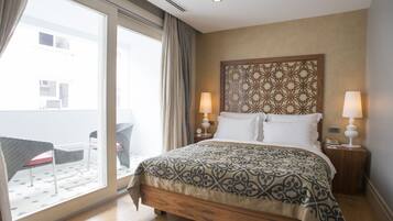 Quarto de hotel com uma cama grande, duas luminárias de cabeceira, um painel de cabeceira estampado e vista para a varanda externa.