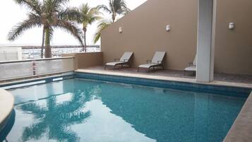 Uma piscina com água cristalina, rodeada por espreguiçadeiras e palmeiras, indicando um ambiente de resort.