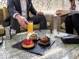 Uma mesa com uma câmera, um copo de suco de laranja e três sobremesas.