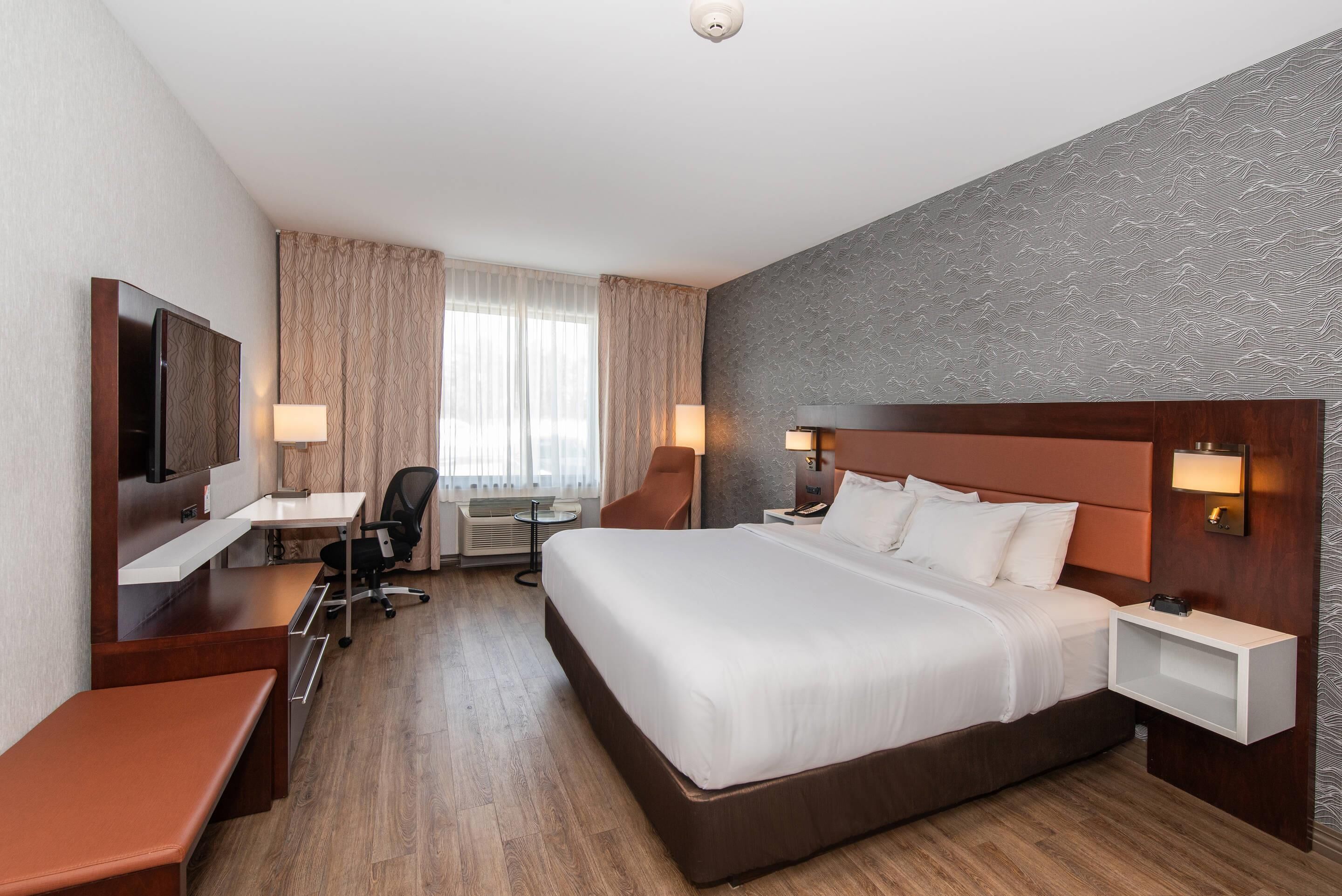 Quarto de hotel com cama, escrivaninha, cadeira, televisão e vista para o exterior.