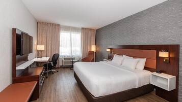 Quarto de hotel com cama, escrivaninha, cadeira, televisão e vista para o exterior.