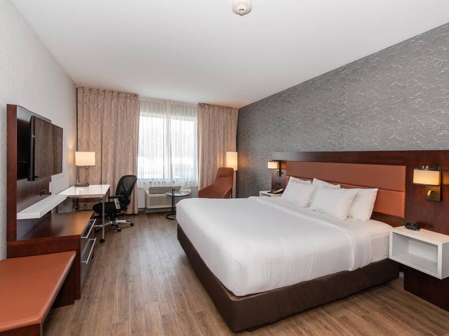 Quarto de hotel com cama, escrivaninha, cadeira, televisão e vista para o exterior.