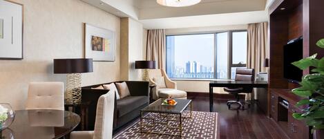 Quarto de hotel moderno com uma janela grande que oferece vista da cidade, um sofá, uma mesa de jantar e uma televisão.