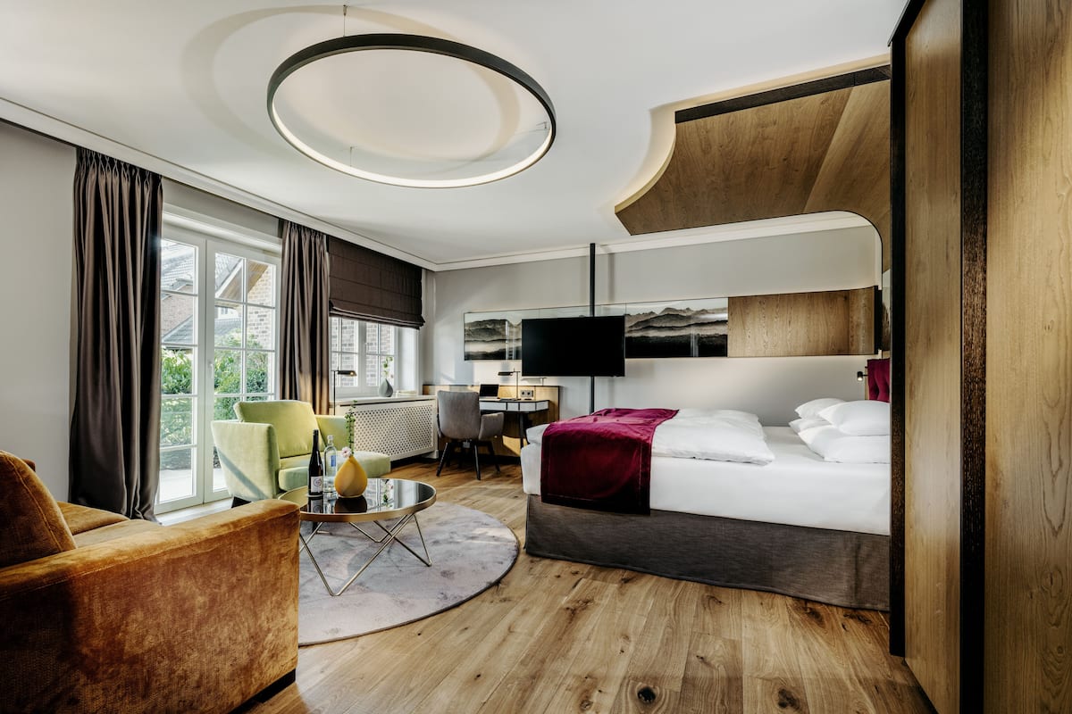 Quarto de hotel moderno com cama, escrivaninha, poltrona, televisão e vista para o exterior.