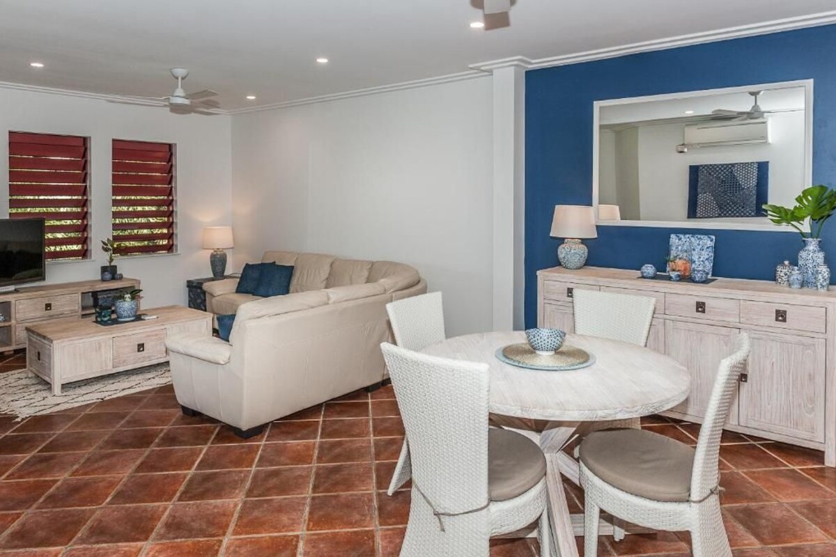 Uma sala de estar com sofá, mesa de jantar, cadeiras, TV e um armário.
