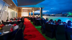 Uma sala de banquetes com mesas montadas para um evento formal, tapete vermelho e vista para a cidade.