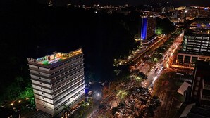 Um hotel com vários andares e um bar no terraço, rodeado por uma rua urbana movimentada à noite.
