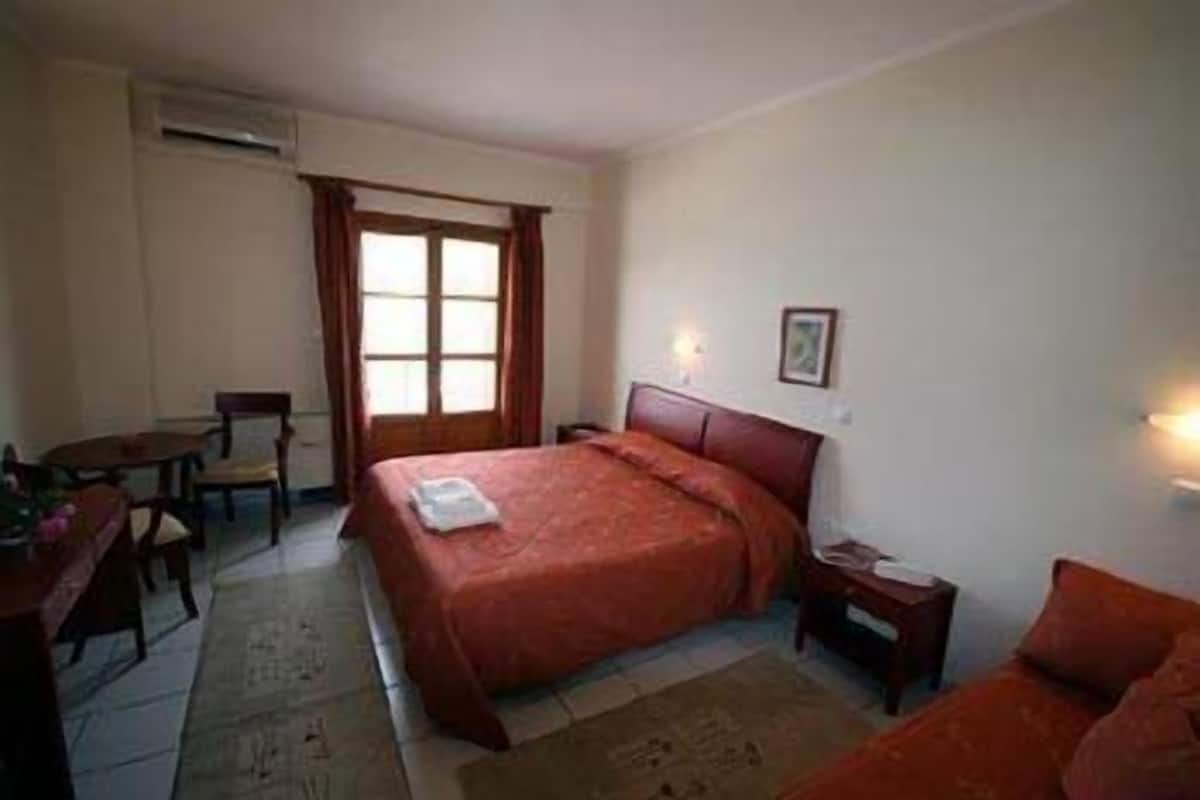 Quarto de hotel com cama, escrivaninha, cadeira, mesa de cabeceira e janela com cortinas.