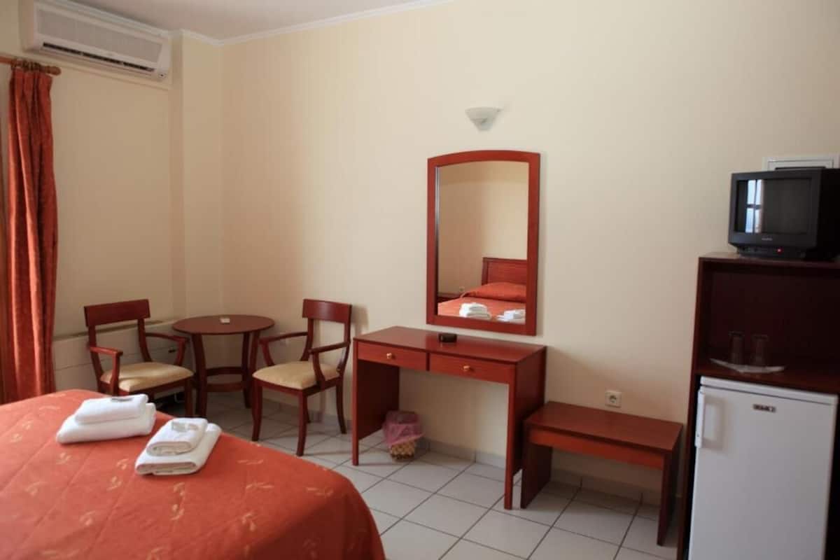 Quarto de hotel com cama, escrivaninha, cadeira, mesa pequena, televisão e frigorífico.